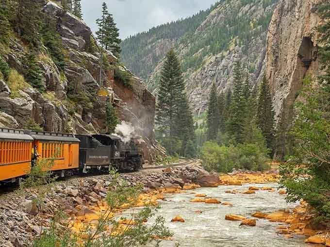 That orange-tinted water tells stories of minerals and mountains while the steam engine writes its own chapter above.