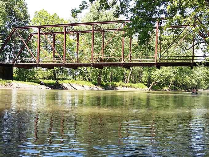 From the creek below, the bridge spans like a rusty rainbow, its reflection rippling across water that's seen decades pass.