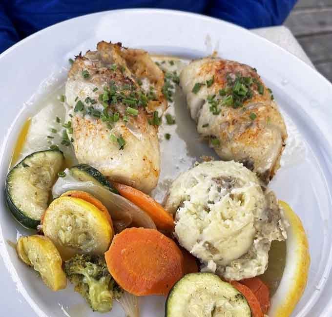 Baked stuffed flounder arrives like a golden treasure, surrounded by perfectly roasted vegetables that actually taste like vegetables should taste.