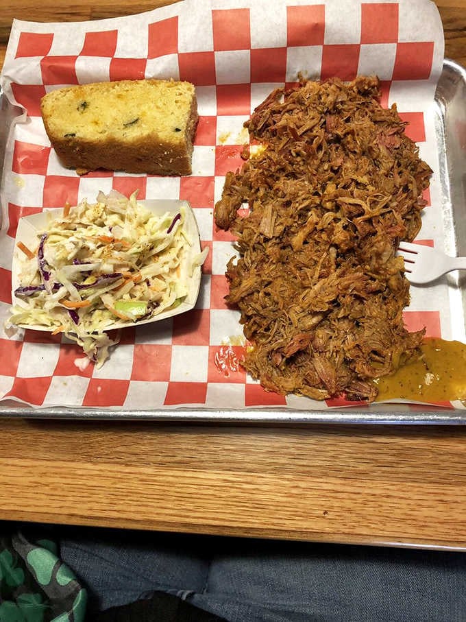 Pulled pork piled high enough to require architectural support, with coleslaw and cornbread playing perfect supporting roles.