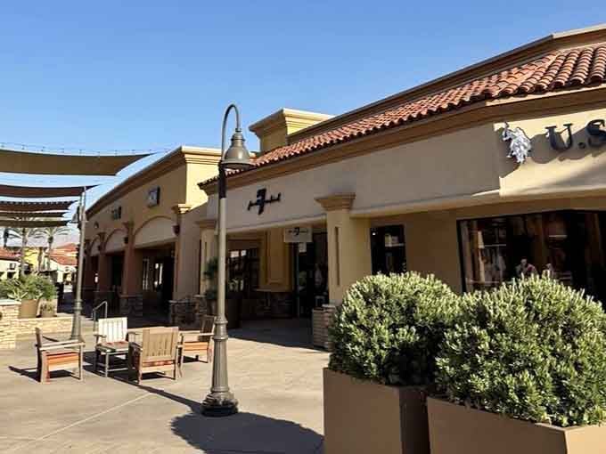 Outdoor shopping oasis with Spanish-style architecture, wooden benches, and manicured planters inviting leisurely afternoon strolls.