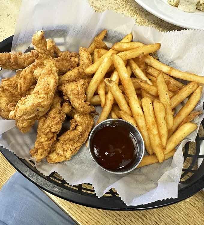 Golden fried chicken tenders with fries that could make a vegetarian reconsider their entire life philosophy, served with sauce for maximum happiness.