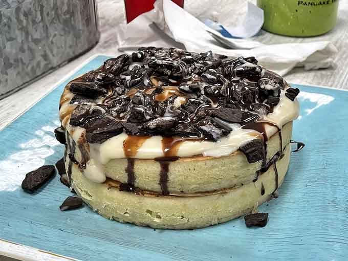 The Oreo pancake towers over the plate like a delicious skyscraper drizzled with chocolate and sweet cream glory.