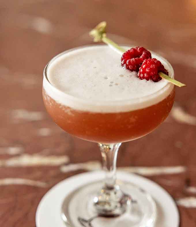 Fresh raspberries garnish this cocktail like tiny jewels, making happy hour feel downright fancy.