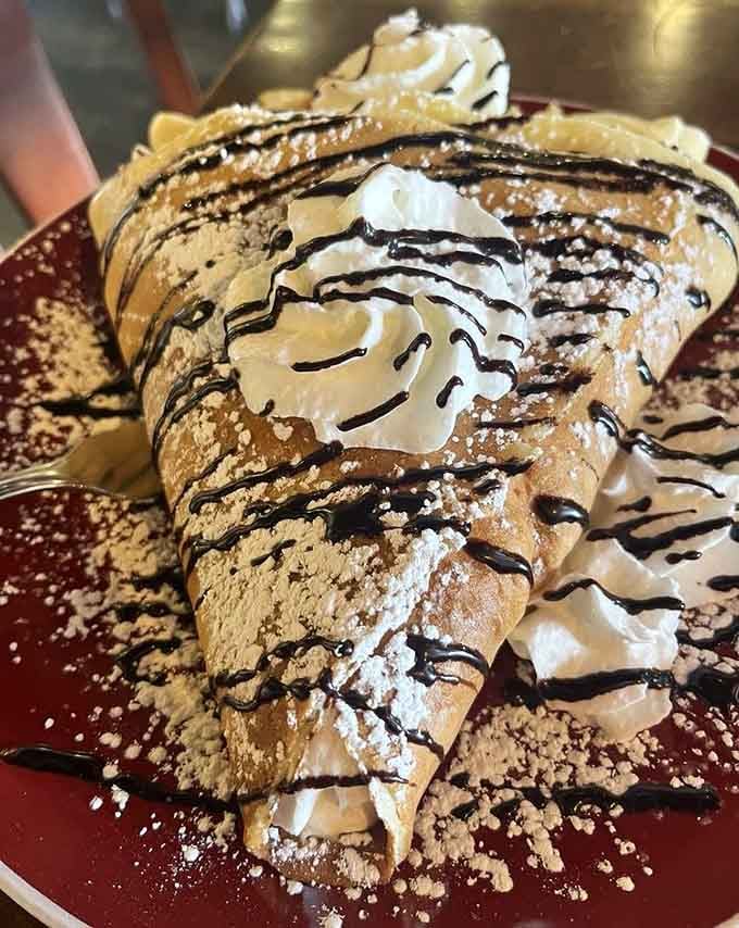 This crepe is dressed to impress with whipped cream, chocolate drizzle, and enough powdered sugar to make Mary Poppins jealous.