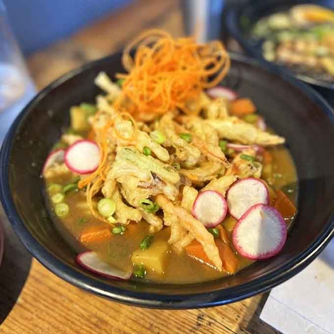 Curry udon arrives as a golden bowl of comfort, topped with crispy garnishes and radishes for textural perfection.