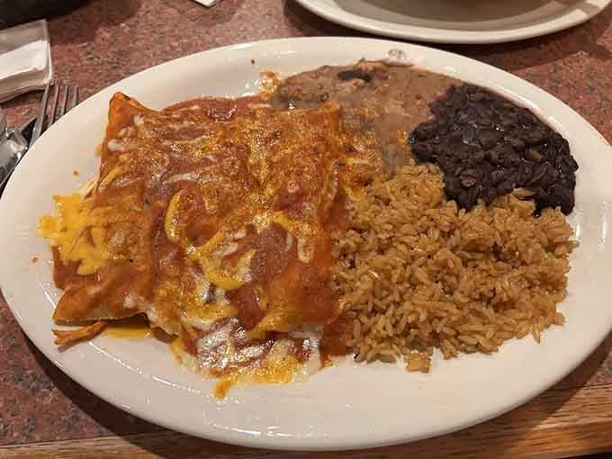 Three enchiladas blanketed in sauce and cheese, flanked by rice and beans that could headline their own show.