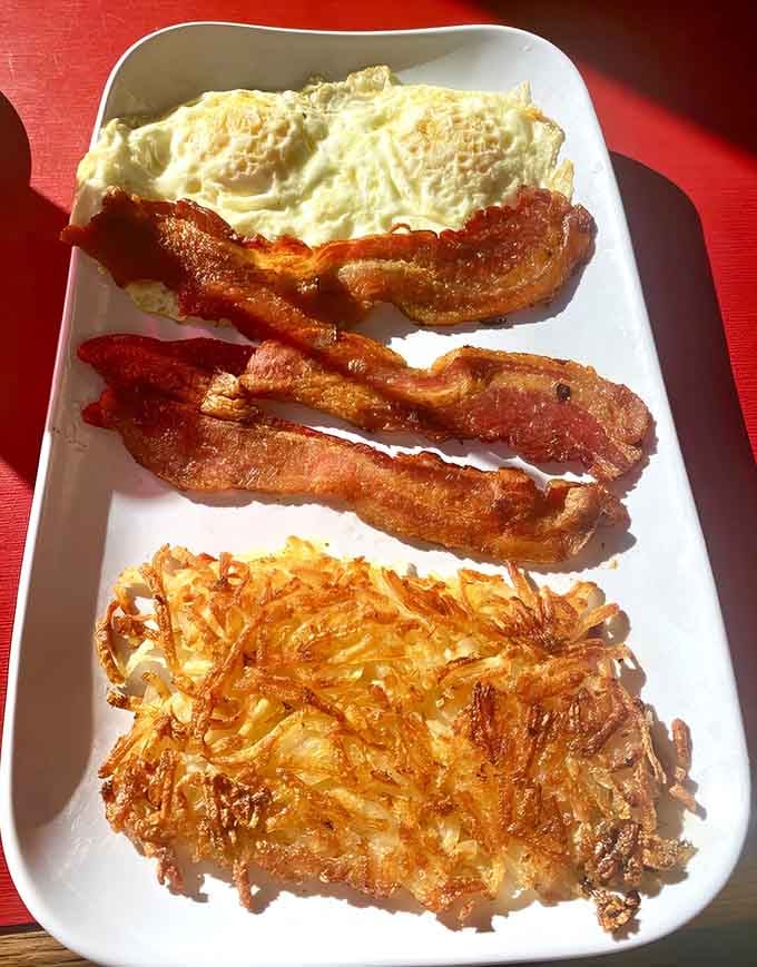 Golden hashbrowns, perfectly cooked eggs, and crispy bacon arranged like edible art on your plate.