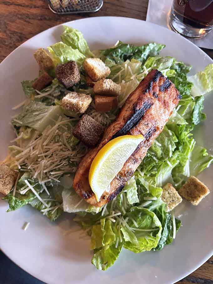 Grilled salmon perched atop Caesar salad like it just conquered Mount Delicious and planted its flag.