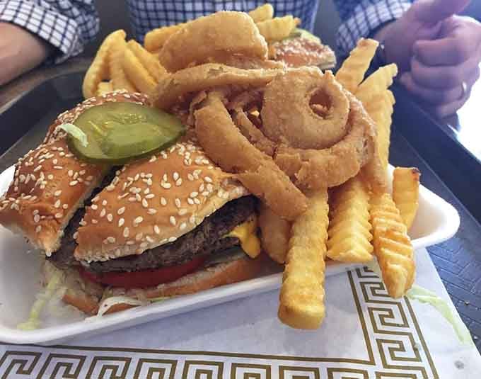 Look at that sesame seed bun cradling a juicy patty, crispy onion rings, and golden fries piled high like edible treasure.