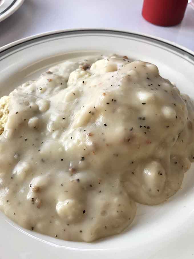 Behold: biscuits drowning in sausage gravy at The Gem Diner, defying all known laws of portion control.
