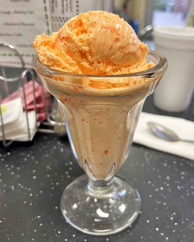 Orange pineapple ice cream served in a proper glass dish, because some traditions refuse to be improved upon.