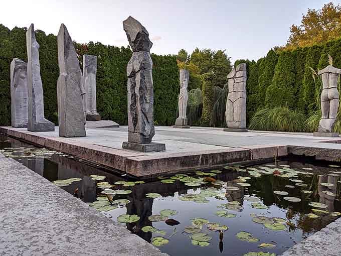 Towering sculptures rise from reflecting pools like ancient monoliths, creating a contemplative space where art meets tranquility.