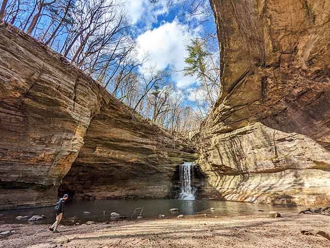 Canyon walls soar upward as a delicate waterfall cascades into a crystal-clear pool surrounded by striped limestone layers.