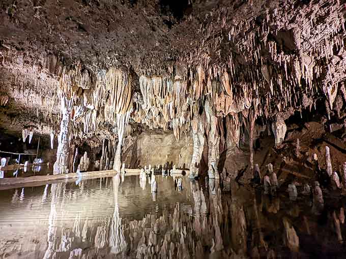 Underground chambers adorned with stalactites and stalagmites create a mirror-perfect reflection in the still cave pool below.