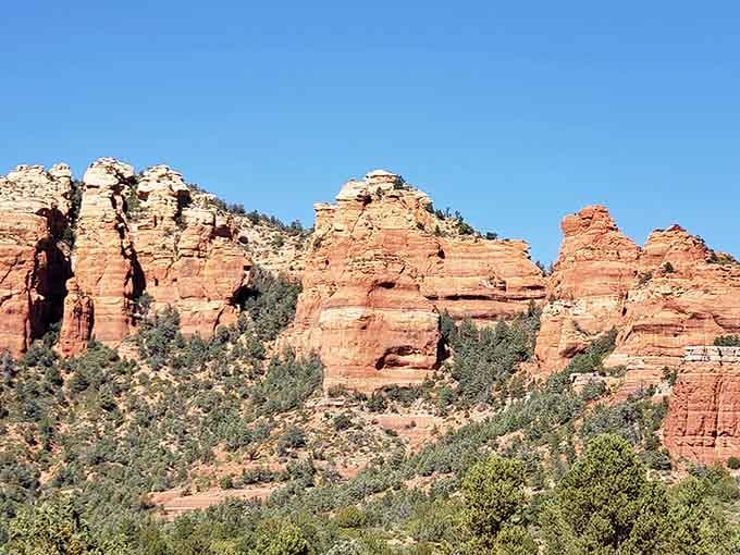 The layered red rock formations of Oak Creek Canyon rise majestically above the lush green trees below in Sedona.