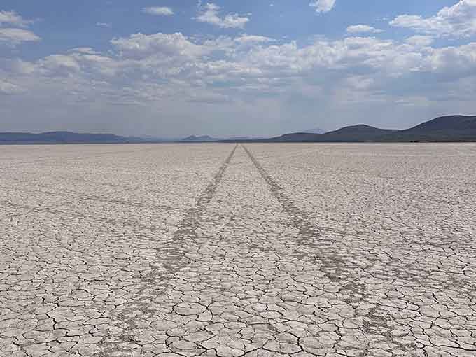 Tire tracks stretch toward distant mountains across a cracked desert floor that goes on forever and ever.