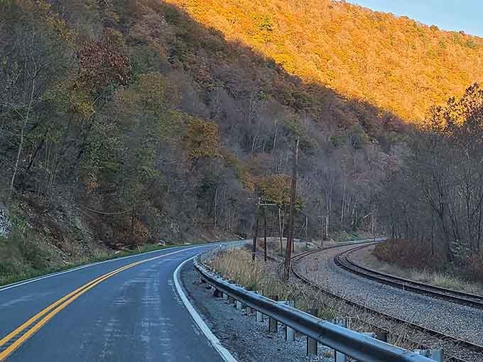 The mountainside glows like molten gold at sunset while the road curves alongside old railroad tracks below.