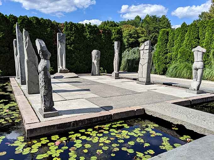 Lily pads float peacefully around modern stone figures, blending natural beauty with human creativity in perfect harmony.