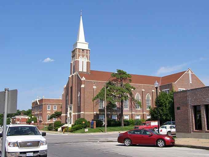 A brick church spire reaches skyward while cars pass below, blending spiritual beauty with everyday life seamlessly.