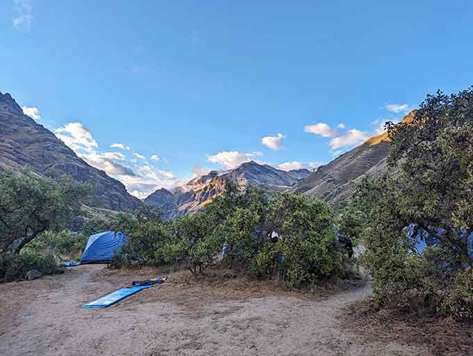 Mountain peaks frame a riverside campsite where nature provides better entertainment than any television ever could back home.