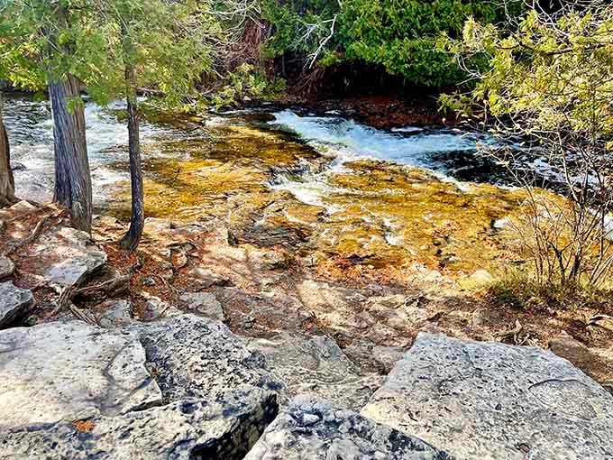 Amber-tinted pools catch the light as water tumbles gently over layered rock formations in peaceful rhythm.