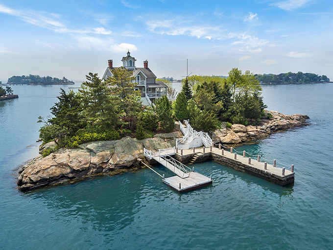 A charming Victorian house perches on its own private island, connected by a white wooden walkway.