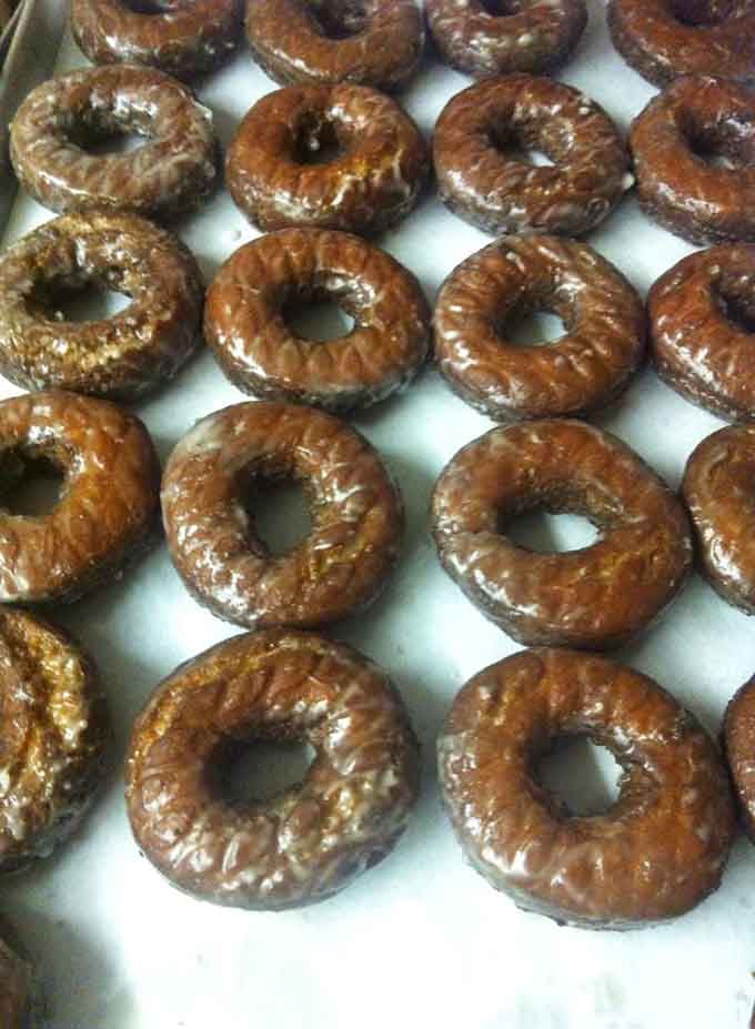 Fresh glazed donuts cooling on the tray, each one a perfect circle of possibility waiting to make someone's morning infinitely better.