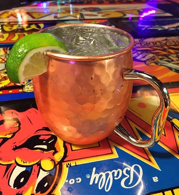 That copper mug glow means Moscow Mule time, perfectly positioned on a vintage arcade cabinet for maximum nostalgia.