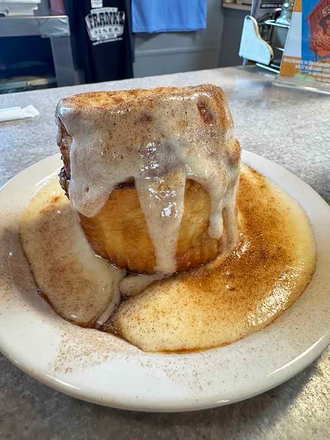 That cinnamon roll towers like a sweet skyscraper, dripping with glaze that cascades down like a delicious waterfall of morning joy.
