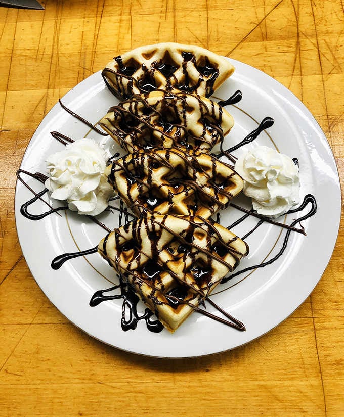 Chocolate drizzle and whipped cream transform simple waffles into a dessert-worthy breakfast that defies all dietary logic.