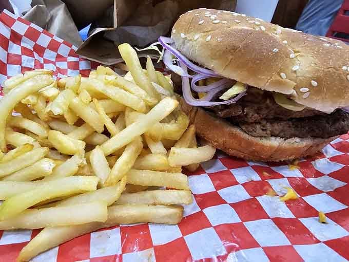 That sesame-seed bun cradles a juicy burger alongside golden fries on classic checkered paper, pure roadside perfection achieved.