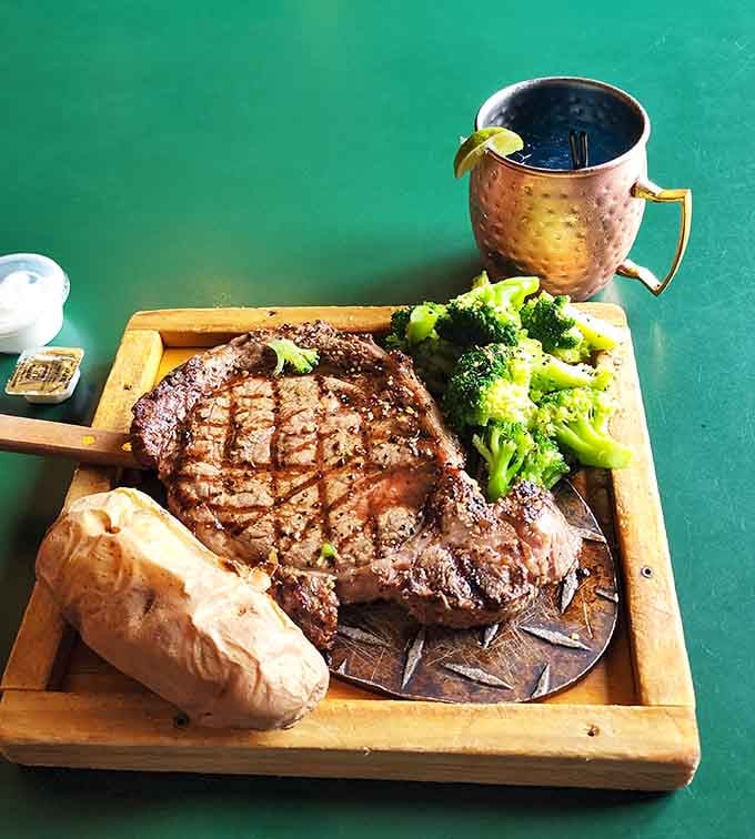 That steak arrives on a wooden board like edible treasure, complete with a copper mug for maximum rustic points.