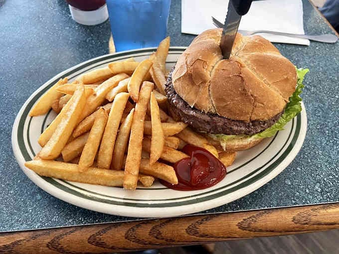 A burger so generously portioned it requires architectural planning before that first bite, fries standing guard on the side.
