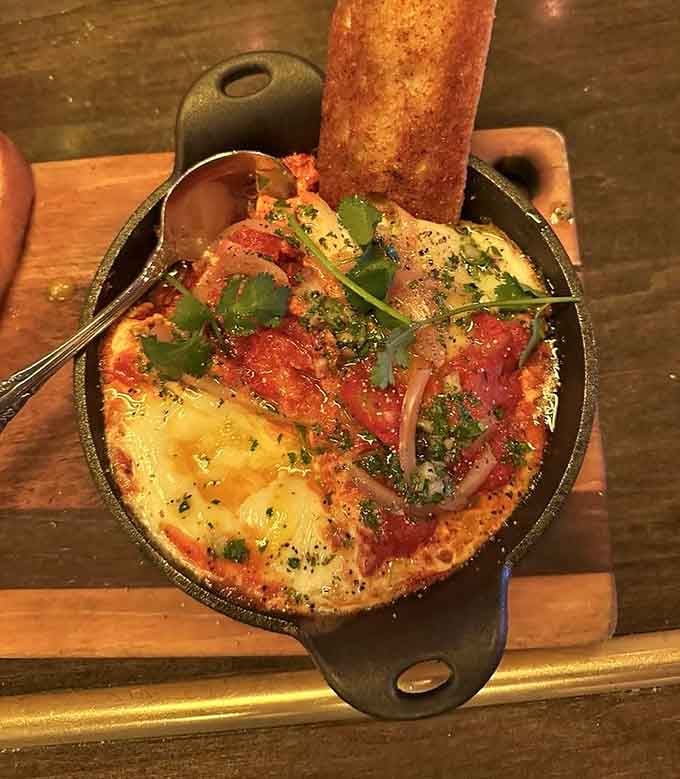 Shakshuka arrives in a cast-iron skillet, bubbling with eggs, tomatoes, and enough flavor to wake up your taste buds.