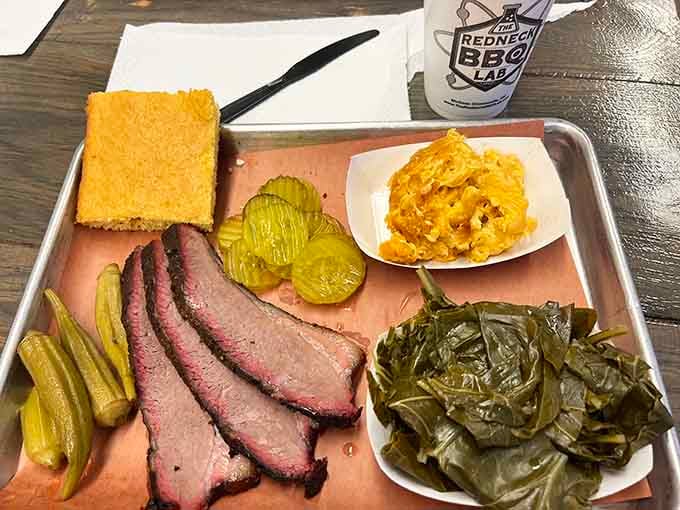 Perfectly sliced brisket with that telltale smoke ring and bark, flanked by pickles and cornbread like edible bodyguards.