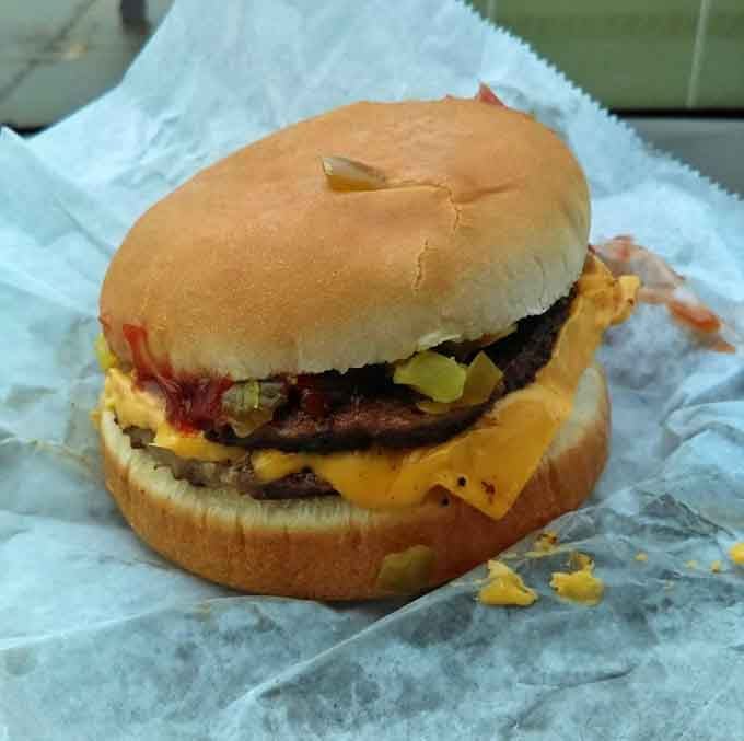 That double cheeseburger with pickles peeking out is what dreams are made of, wrapped in simple paper.