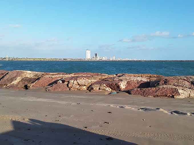 Where the Gulf meets the shore, weathered rocks frame a view of distant civilization across pristine waters.