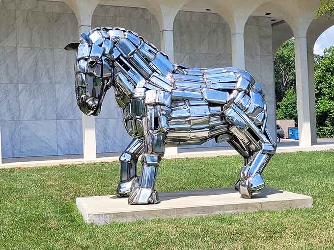 This chrome horse gleams like a futuristic knight's steed, reflecting clouds and trees in its polished metallic surface.