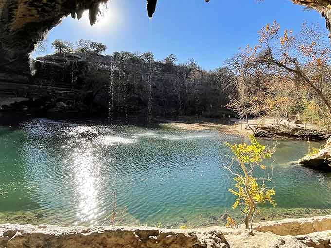 Crystal-clear water pools beneath a natural grotto, where stalactites drip like nature's own chandelier above emerald depths.