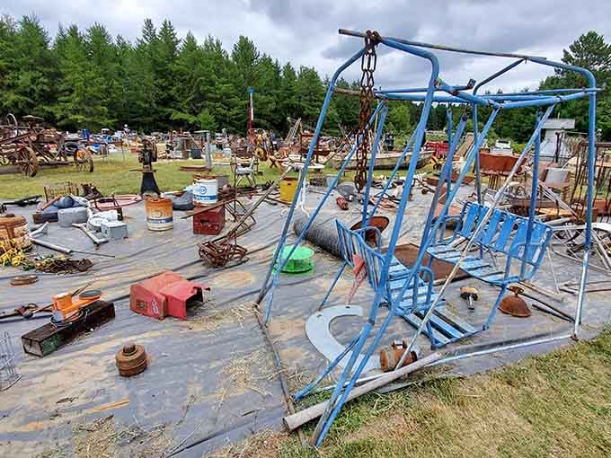 That weathered blue swing set frame stands like modern art among the rusty relics and vintage tools.