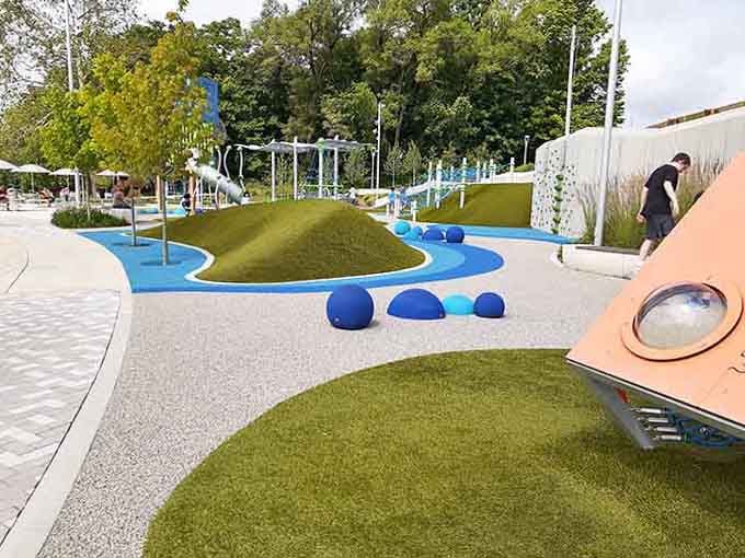 Modern playground design meets artistic vision in rolling hills of green and flowing paths of cheerful bright blue.