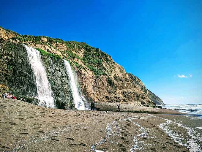 Twin waterfalls cascade down moss-covered cliffs straight onto the beach, because California doesn't believe in doing things halfway.