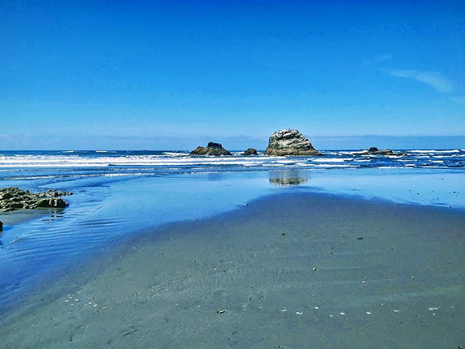 Sea stacks rise from shallow waters like ancient sentinels, their reflections doubling the coastal drama perfectly.