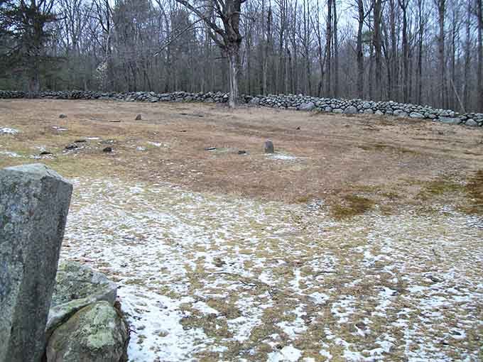 Stone walls encircle this quiet burial ground where winter's bare trees and scattered snow add to the eerie atmosphere.