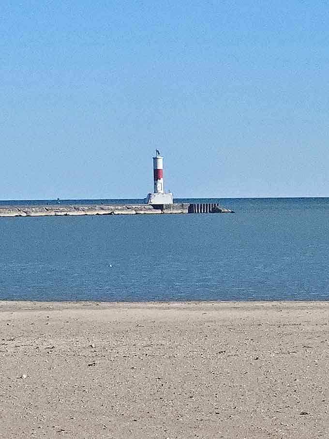 The lonely lighthouse stands watch at pier's end, a solitary sentinel framed by endless blue water and sky.