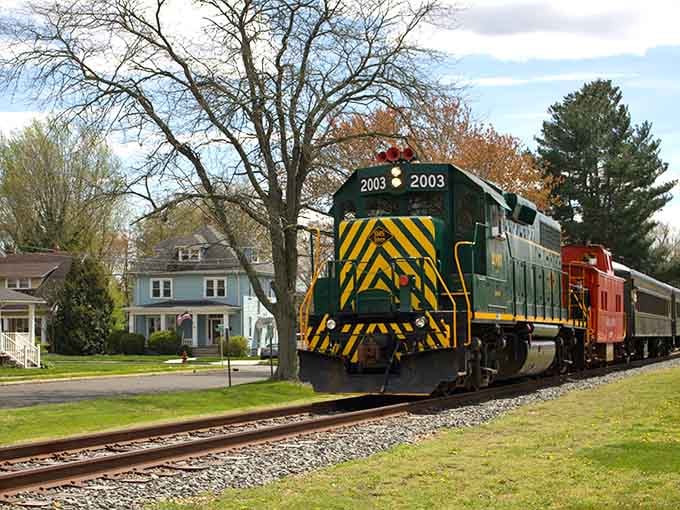 Diesel locomotive 2003 rolls through a quiet neighborhood where trains and houses coexist like old friends.