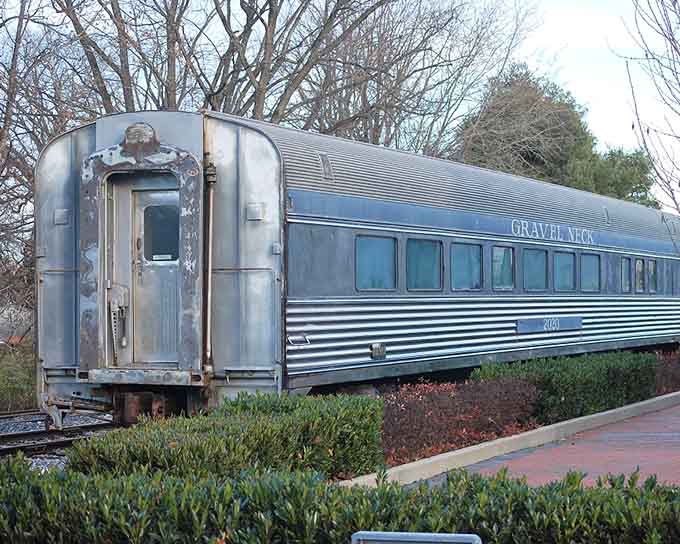 The vintage silver passenger car rests peacefully in landscaped surroundings, retired but dignified like a well-earned vacation after decades of service.