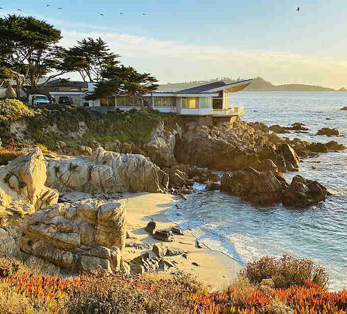 Coastal architecture perched on dramatic cliffs where crashing waves meet golden hour light in perfect California harmony and style.
