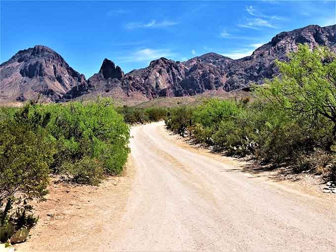 The dusty road curves toward dramatic mountain peaks, beckoning adventurers to explore what lies beyond the next bend.